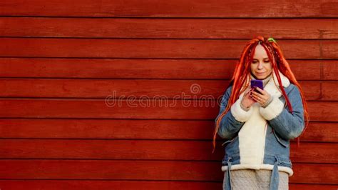 Woman With Orange Dreadlocks And In A Warm Denim Jacket Using