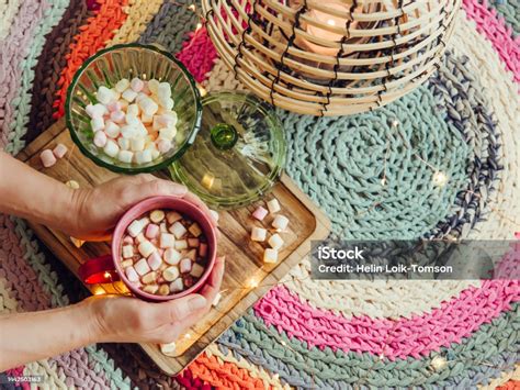 아늑한 겨울날 미니 마시멜로와 함께 빨간 코코아 컵을 들고 있는 여성의 손을 클로즈업한 모습 랜턴 Led 조명이 타오르고