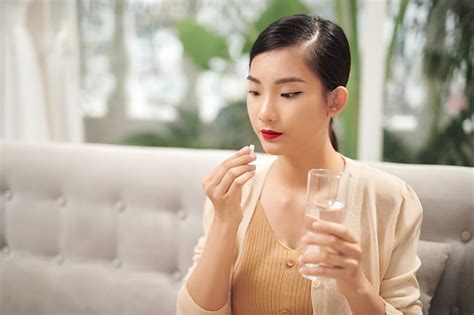 집에서 옷을 입은 아픈 아름다운 소녀가 물 한 잔으로 창문 근처에서 약을 복용합니다 건강관리와 의술에 대한 스톡 사진 및 기타 이미지 건강관리와 의술 건강한 생활방식