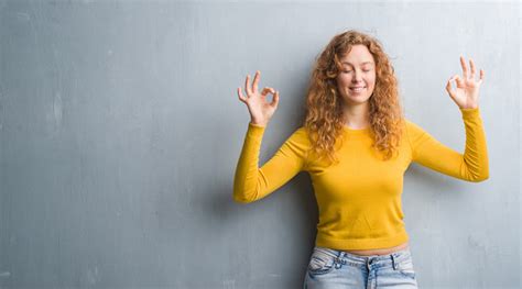 젊은 빨강 머리 여자 회색 그런 지 벽에 휴식과 명상 손가락으로 제스처를 하 고 폐쇄 눈으로 웃 고 요가 개념 개념에 대한 스톡