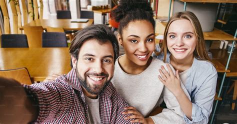 캐주얼 복장을 입은 세 명의 웃는 젊은 사업가들이 미소를 지으며 자신을 촬영합니다 사무실 인테리어 배경에 책꽂이 성공의 개념 사진 Unsplash의 우정 이미지