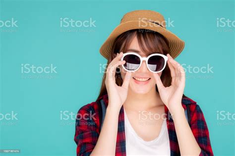 아름다운 초상화 젊은 아시아 여성은 모자를 착용하고 파란색 배경에 고립 된 휴가 여름 여행을 즐길 자신감 선글라스를 들고 여행과