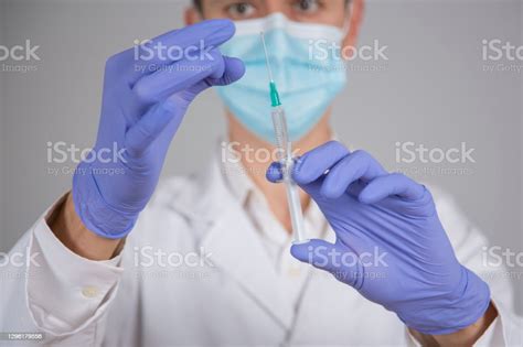 흰색 코트와 파란색 마스크의 의사가 회색 배경에 코로나 바이러스 백신 주사기를 손에 들고 40 44세에 대한 스톡 사진 및 기타