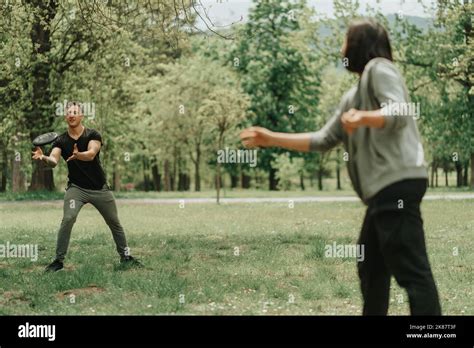 Sport Girl Throwing Frisbee To Her Babefriend While Standing In The Park And The Babe Catching It