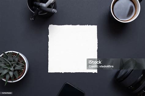 전화 카메라 커피 머그잔 식물 및 펜으로 둘러싸인 검은 사무실 책상에 빈 종이 프레임 평면도 복사 프레젠테이션을 위한 플랫 레이