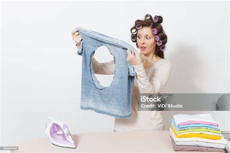 미친 주부 Curlers 들고 가벼운 옷에 머리에 구운 셔츠 다림 질 보드에 서 서 쇠에 의해 만든 구멍 충격된 재미 흰색 배경에 고립 된 여자입니다 광고에 대 한 공간을