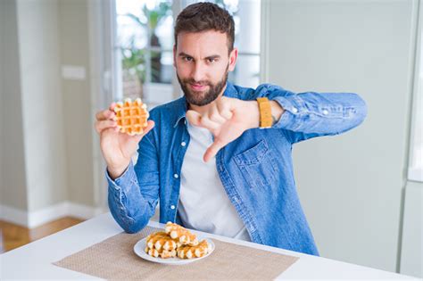 화가 난 얼굴로 달콤한 벨기에 팬케이크를 먹는 잘생긴 남자 엄지 손가락으로 싫어하는 것을 보여주는 부정적인 표지판 거부 개념