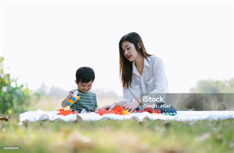 젊은 아시아 어머니와 귀여운 작은 아들의 초상화는 여름 공원에서 화창한 하루를 보내고 화려한 플라스틱 블록 장난감을 연주하는 풀밭에 앉아 있습니다 행복한 가족은 장난감을
