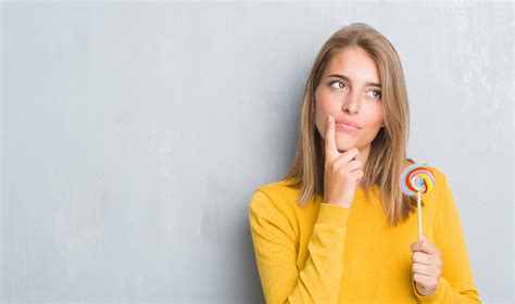 그런 지 회색에 아름 다운 젊은 여자 먹는 롤리팝 사탕 심각한 얼굴 생각 질문 매우 혼란 스 러 워 아이디어에 대 한 벽 개념에 대한 스톡 사진 및 기타 이미지 Istock