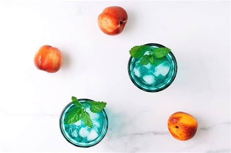 차가운 음료와 얼음 조각이있는 아름다운 빈티지 청록색 안경 2 개와 신선한 녹색 민트 잎과 흰색 대리석 테이블에 3 개의 넥타린이 장식되어 있습니다 0명에 대한 스톡 사진