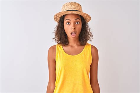 노란 티셔츠와 여름 모자를 쓰고 고립된 흰색 배경에 노란색 티셔츠와 여름 모자를 쓰고 있는 젊은 브라질 여성은 깜짝 표정과 두려움 흥분된 얼굴로 충격을 받았다 T 셔츠에