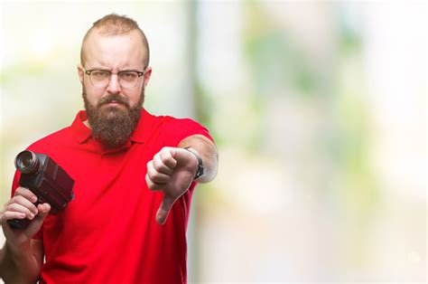 젊은 백인 Hipster 남자 Filmming 레트로 비디오 카메라를 사용 하 여 성 난 얼굴 아래로 엄지 싫어 보여주는 음수 부호 거부 개념 고립 된 배경 위에 개념에