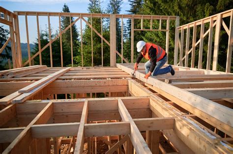 Carpenter Hammering Nail While Constructing Wooden Frame Two Story House Near The Forest Stock