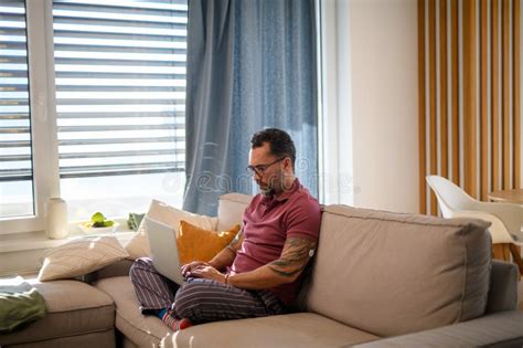 Man With Cgm Sensor On Arm Sitting On Sofa And Working On Laptop Stock