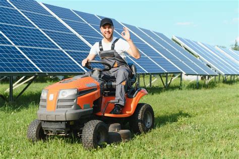 A Man Working At Solar Power Station A Worker On A Garden Tractor Mows