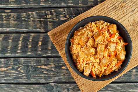 검은 그릇에 고기와 당근을 곁들인 필라프 검은 색 배경에 필라프 초라한 테이블에 음식 오래된 나무 판에 그릇 음식과 가까운 텍스트를 위한 공간과 여유 공간을 복사합니다