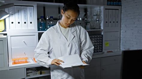A Focused Asian Woman Scientist In A Lab Coat Analyzing Documents In A