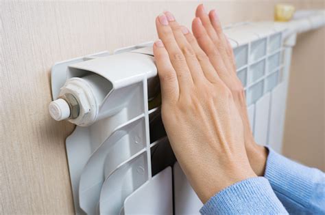 한 여성이 방에 있는 집에서 히터인 배터리 위에 손을 따뜻하게 합니다 손가락 손바닥은 라디에이터에서 따뜻하게 유지 가까이 낮은 실온 겨울 난방 기간 계절 가정 난방에 대한