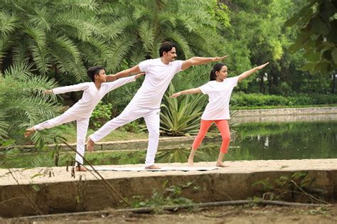행복한 젊은 남성 인도 가정교사가 두 명의 행복한 어린 아이들에게 명상과 운동 요가 포즈를 취하는 방법을 가르치고 이른 아침 공원에서 녹색의 고요한 환경에서 요가를 합니다