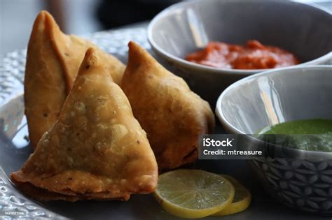 민트 고수풀 딥과 토마토 처트니 라메킨과 함께 제공되는 매운 감자 완두콩 고기로 채워진 튀긴 사모사의 회색 접시가 있는 레스토랑 테이블의 전체 프레임 이미지 전경에 초점