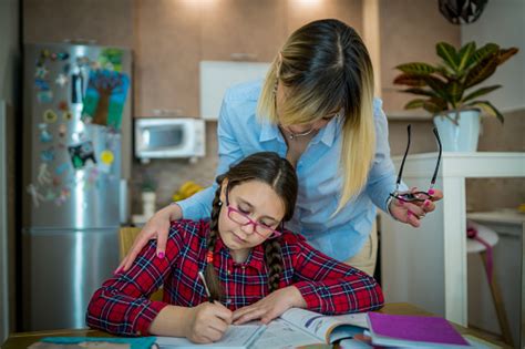 매력적인 젊은 여성과 그녀의 작은 귀여운 딸은 테이블에 앉아 함께 숙제를하고있습니다 어머니는 딸이 학교 수업을 하도록 도와줍니다