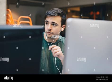 Thoughtful Computer Programmer Wearing In Ear Headphones In Office