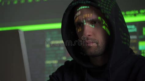Male Hacker Working On A Computer While Green Code Characters Reflect