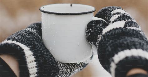 겨울에는 마른 풀과 눈 호수를 배경으로 따뜻한 차 한 잔을 들고 아늑한 장갑을 끼고 있습니다 추운 겨울에 하이킹과 여행 따뜻한 음료 텍스트를 위한 공간 사진