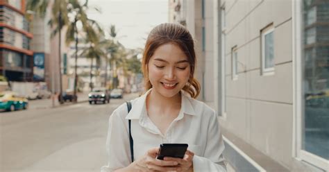 스마트폰을 사용하여 패션 사무복을 입고 아침에 도시의 현대 도시에서 혼자 야외를 걷는 동안 문자 메시지를 입력하는 성공적인 젊은 아시아 사업가 이동 중 비즈니스 개념