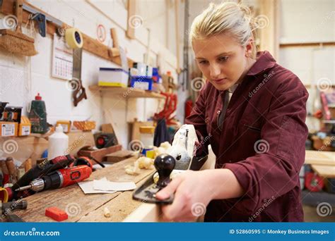 Female Apprentice Planing Wood In Carpentry Workshop Stock Image