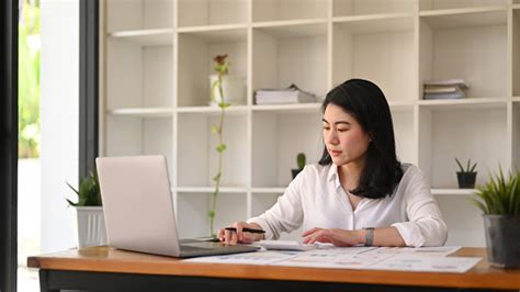 집중적 인 여성 경제학자는 재무 문서의 수치 데이터를 검사하고 사무실 책상에서 랩톱 컴퓨터를 사용합니다 25 29세에 대한 스톡