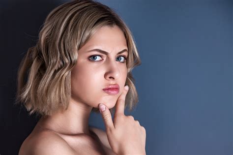 불만족스러운 표정으로 화난 여자의 초상화를 클로즈업하고 어두운 회색 배경에서 포즈를 취하고 카메라를 바라본다 빈 스튜디오 벽에