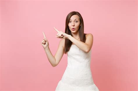하얀 웨딩에서 놀된 신부 여자의 초상화는 서 부 입술 옆으로 파스텔 핑크 배경에 고립 된 인덱스 손가락을 가리키는 드레스 결혼식 축 하 개념입니다 광고에 대 한 공간을 복사