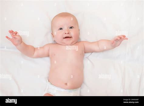 A Smiling Baby On A White Bed Infant Baby Girl Spreading Arms In