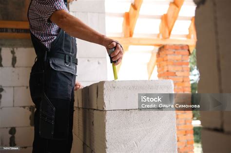 건설 현장의 건설 작업자는 테이프 측정으로 창 개구부 및 벽돌 벽의 길이를 측정합니다 코티지는 다공성 콘크리트 블록 작업복으로