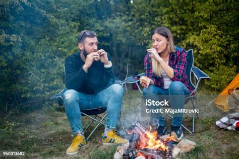 아름 다운 커플 앉아 캠프 파이어 주위에 캠핑 텐트와 배경에 남자 막대기로 화재 제스처 건강한 생활방식에 대한 스톡 사진 및 기타 이미지 Istock