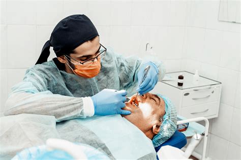 젊은 남성 치과 의사가 환자를 치료합니다 치과 수술에서 의료 조작 전문 유니폼 과 치과 의사의 장비 의사의 직장을 갖추는 의료