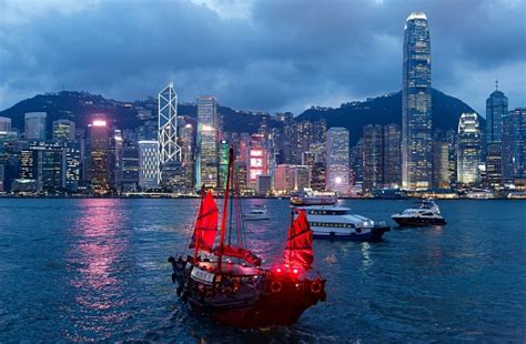 붐비는 고층 빌딩 사이에 서 있는 Ifc 타워 물에 반사된 고층 건물의 눈부신 불빛 해질녘 순항하는 중국 정크 스타일의 관광 보트가 있는 빅토리아 항구 옆 홍콩의 야경