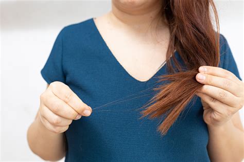 파란 셔츠를 입은 알아볼 수 없는 긴 빨간 머리 여자는 손에 머리카락을 잔뜩 들고 하얀 스튜디오에서 머리 아이템 하나를 돌린다