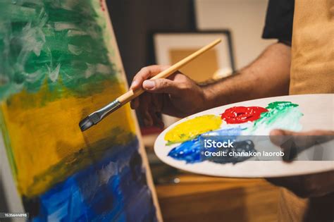 암실에 있는 아시아의 남자는 따뜻한 조명 예술가가 붓과 다양한 아크릴 색으로 그림을 그리는 작업을 하고 있다 예술 개념으로 크리에이티브 스튜디오에서 캔버스에 있는 남자