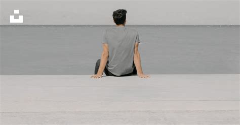 노란 셔츠와 검은 반바지를 입은 남자가 물가 근처의 하얀 모래 위에 앉아 있다 사진 Unsplash의 무료 회색 이미지