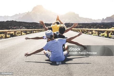 긴 길 한가운데에 앉아 팔을 들고 기뻐하는 십대 무리 두 팔을 벌려 휴가를 즐기는 네 명의 십대의 백 뷰 청소년 자유 여행 및 모험 개념 청소년기에 대한 스톡 사진 및 기타