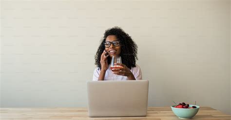 곱슬머리에 초점을 맞춘 흑인 아가씨는 집에서 와인 한 잔과 딸기가 든 그릇이 있는 나무 테이블에서 스마트폰을 사용하여 노트북을 탐색합니다 사진 Unsplash의 마시다 이미지