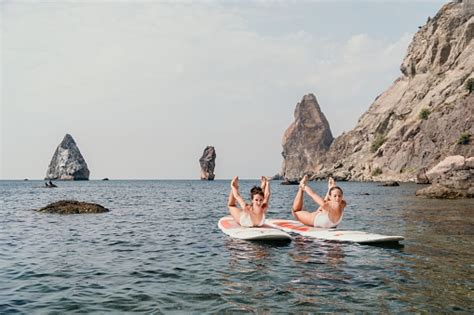 여자는 요가를 한다 패들 섭 서핑보드에서 요가 필라테스를 연습하는 행복한 스포티한 여성 바닷물에서 운동을 하는 여성 스트레칭 현대 개별 여성 힙스터 야외 여름 스포츠 활동