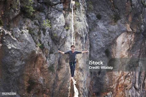 남자는 뻗어 슬링을 따라 걷고 있다 산에서 하이 라인 남자는 균형을 잡는 다 자연에서 줄 타기 워커의 성능 계곡의 배경에 높은