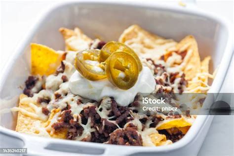 쇠고기 다진 고기와 치즈를 곁들인 나초는 휘핑 크림과 할라 페노스와 함께 제공됩니다 가식적 미소에 대한 스톡 사진 및 기타 이미지 가식적 미소 거품 내기 고기