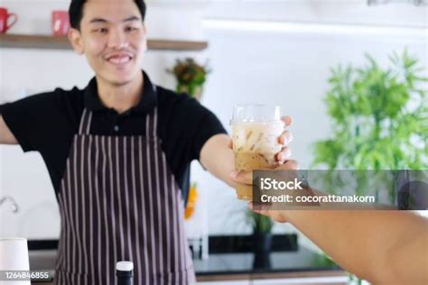 커피숍카운터바에서 아이스 라떼 커피 한 잔을 마시며 미소짓는 아시아 바리스타 청년 투명 플라스틱 유리를 들고 손에 초점을 닫습니다 2명에 대한 스톡 사진 및 기타 이미지