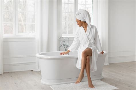 욕조에 앉아있는 흑인 여성 머리에 흰색 목욕 가운과 수건을 착용 집의 가벼운 욕실에서 몸과 피부 관리 여유 공간 전체 길이 20 29세에 대한 스톡 사진 및 기타 이미지