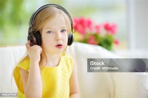 거대한 무선 헤드폰을 착용 하 고 귀여운 소녀입니다 음악을 듣고 있는 예쁜 아이 여학생은 집에서 아이들의 노래를 듣고 재미있게 놀고 있습니다 가정 생활에 대한 스톡 사진 및