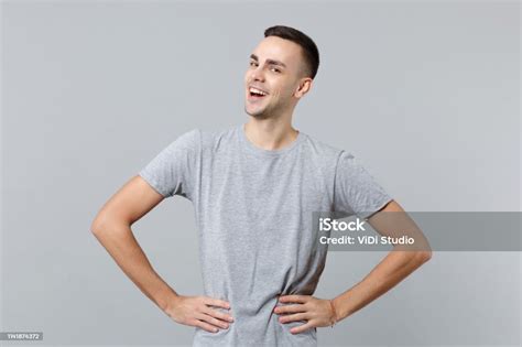 스튜디오에서 회색 벽 배경에 고립 된 허리에 팔 Akimbo에 서 캐주얼 복장 쾌활 한 잘생긴 젊은 남자의 초상화 사람들은 진심으로 감정 라이프 스타일 개념입니다 복사